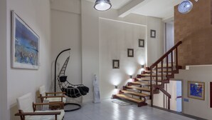 Uma sala ampla com escada de madeira, uma cadeira suspensa e uma estátua.