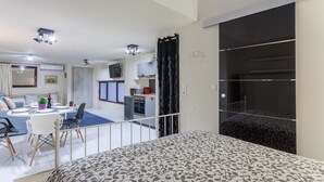 Quarto de hotel moderno com uma cama grande, área de refeições com mesa e cadeiras, cozinha compacta e varanda com vista.