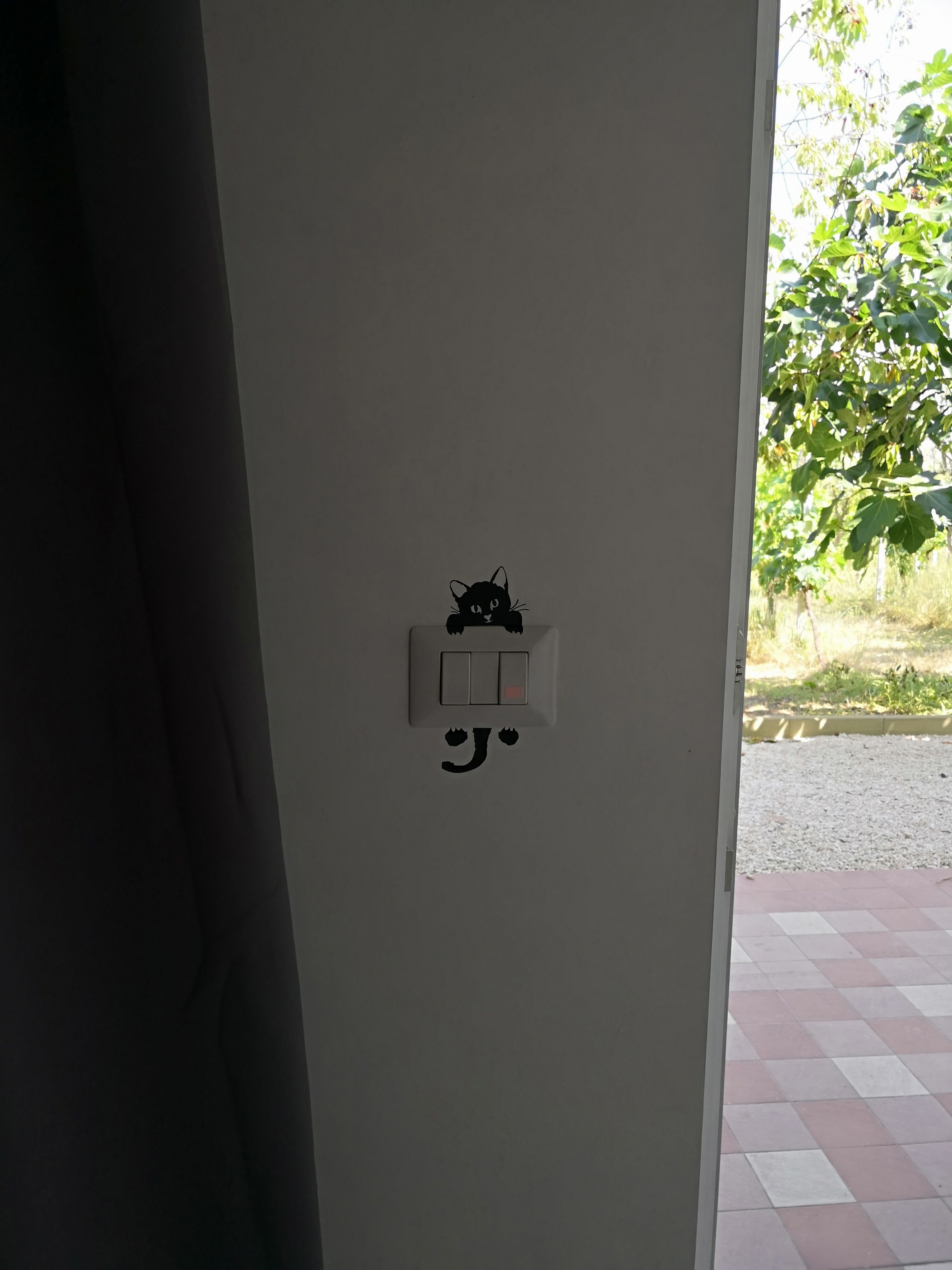 Parede com um interruptor de luz e um adesivo de gato.