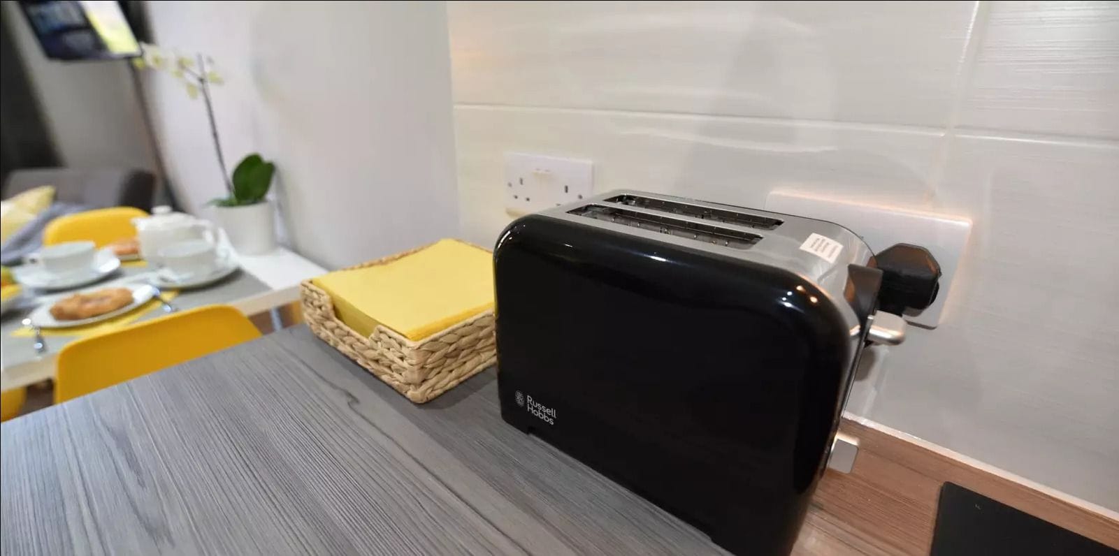 Uma cozinha com uma torradeira preta, um tabuleiro amarelo e uma pequena planta em vaso.