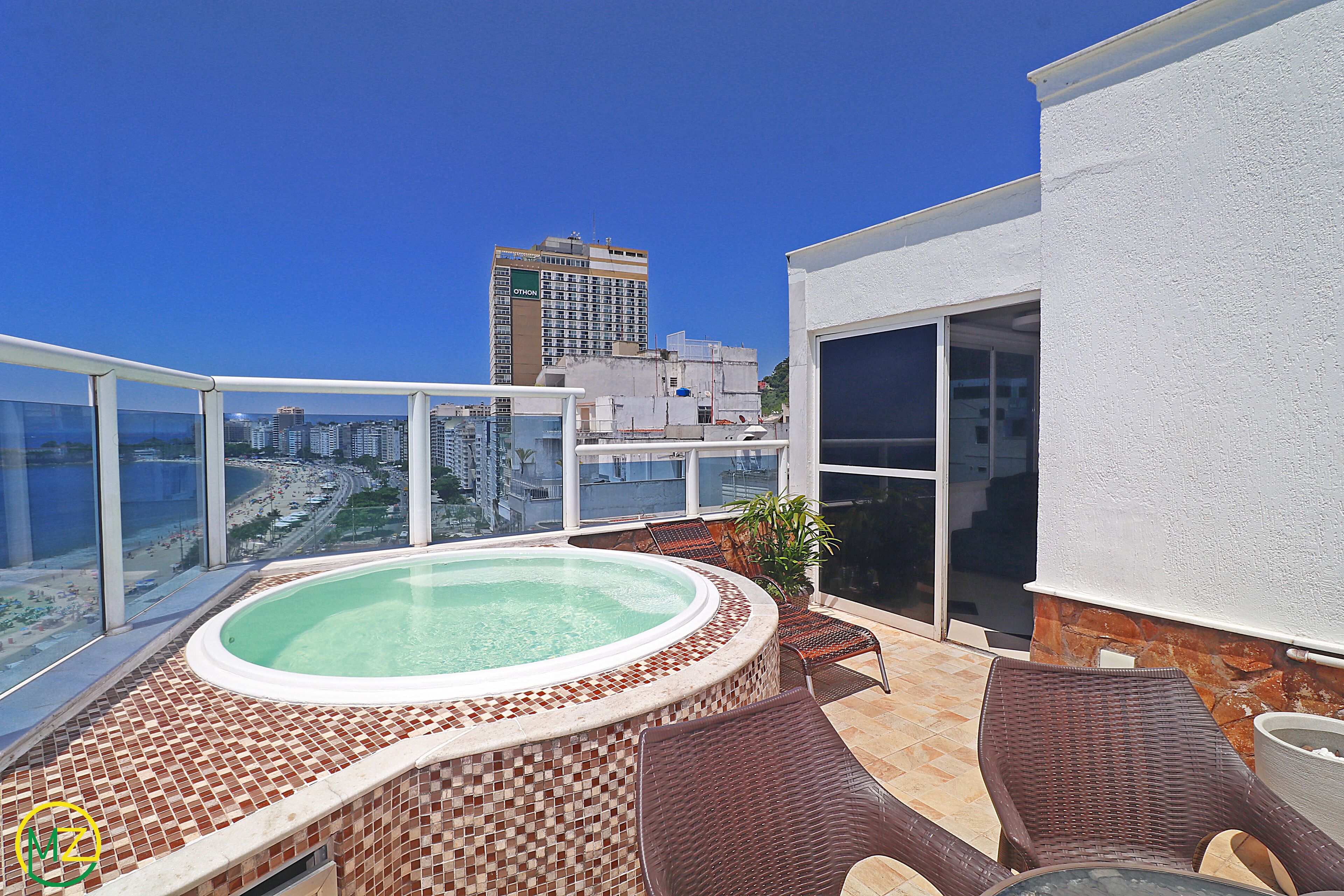 Terraço no telhado com banheira de hidromassagem, cadeiras de vime e vista para o horizonte da cidade.