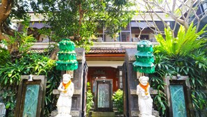Um edifício tradicional com telhado cerâmico, entrada central e estátuas nas laterais da porta.