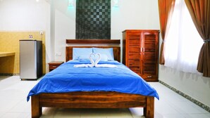 Quarto de hotel com uma cama, guarda-roupa de madeira, uma mesinha e um frigorífico.