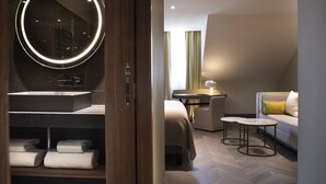 Quarto de hotel moderno com um espelho redondo, uma cama grande, uma mesinha e um sofá.