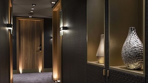 Um corredor com uma porta de madeira, uma luminária na parede e um vaso decorativo.