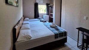 Quarto de hotel com cama, escrivaninha, janela com cortinas e aparelho de ar condicionado.