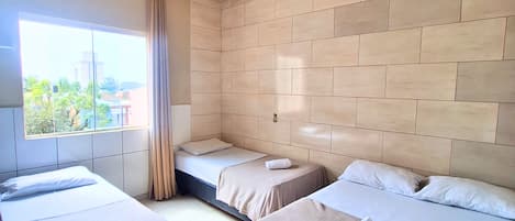 Quarto de hotel com duas camas, uma janela grande e vista para o verde lá fora.