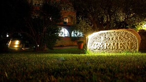 Placa de hotel bem iluminada com o nome 'HOTEL GARMEN' em destaque, rodeada por grama e árvores.