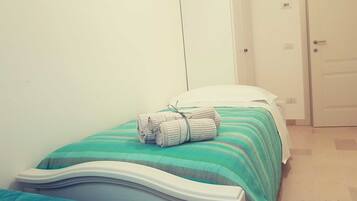 Uma cama de solteiro com uma colcha verde e branca listrada, um travesseiro branco e toalhas dobradas na cama.