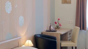 Quarto de hotel com uma cama, uma escrivaninha com cadeira, uma luminária e um painel decorativo na parede.