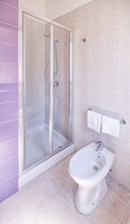 Um banheiro moderno com chuveiro em box de vidro, pia de pedestal e parede revestida com azulejos.