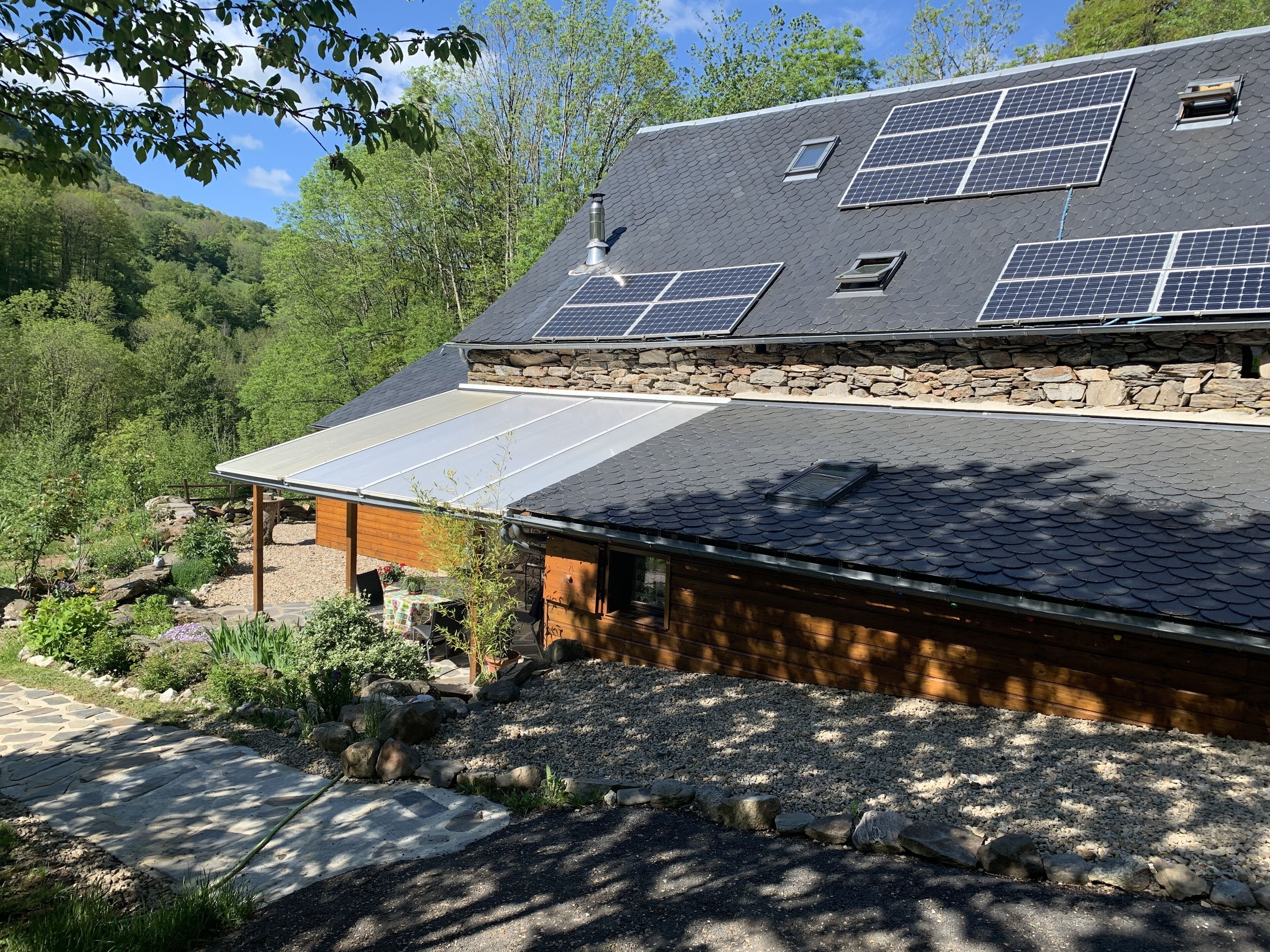 Uma casa com painéis solares, paredes de pedra e um jardim.
