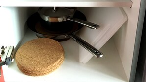 Uma cozinha com utensílios de aço inoxidável na prateleira superior e um bolo de cortiça na prateleira inferior.