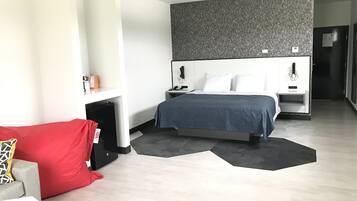 Quarto de hotel moderno com cama, sofá vermelho, mesinha e unidade de armazenamento preta.