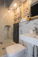 Uma casa de banho moderna com chuveiro em cabine de vidro, sanita branca e lavatório de mármore.