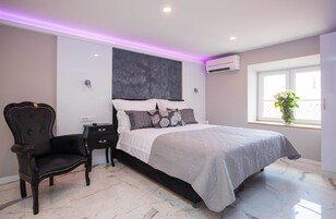 Quarto com cama, mesa de cabeceira, cadeira, janela e ar condicionado.