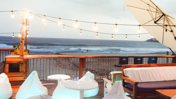 Um terraço com assentos, luzes de festa e vista para o oceano.