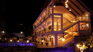 Hotel com vários andares, piscina, área de estar externa e escadaria que dá acesso aos andares superiores.