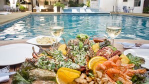 Mesa de jantar com frutos do mar e bebidas à beira de uma piscina.