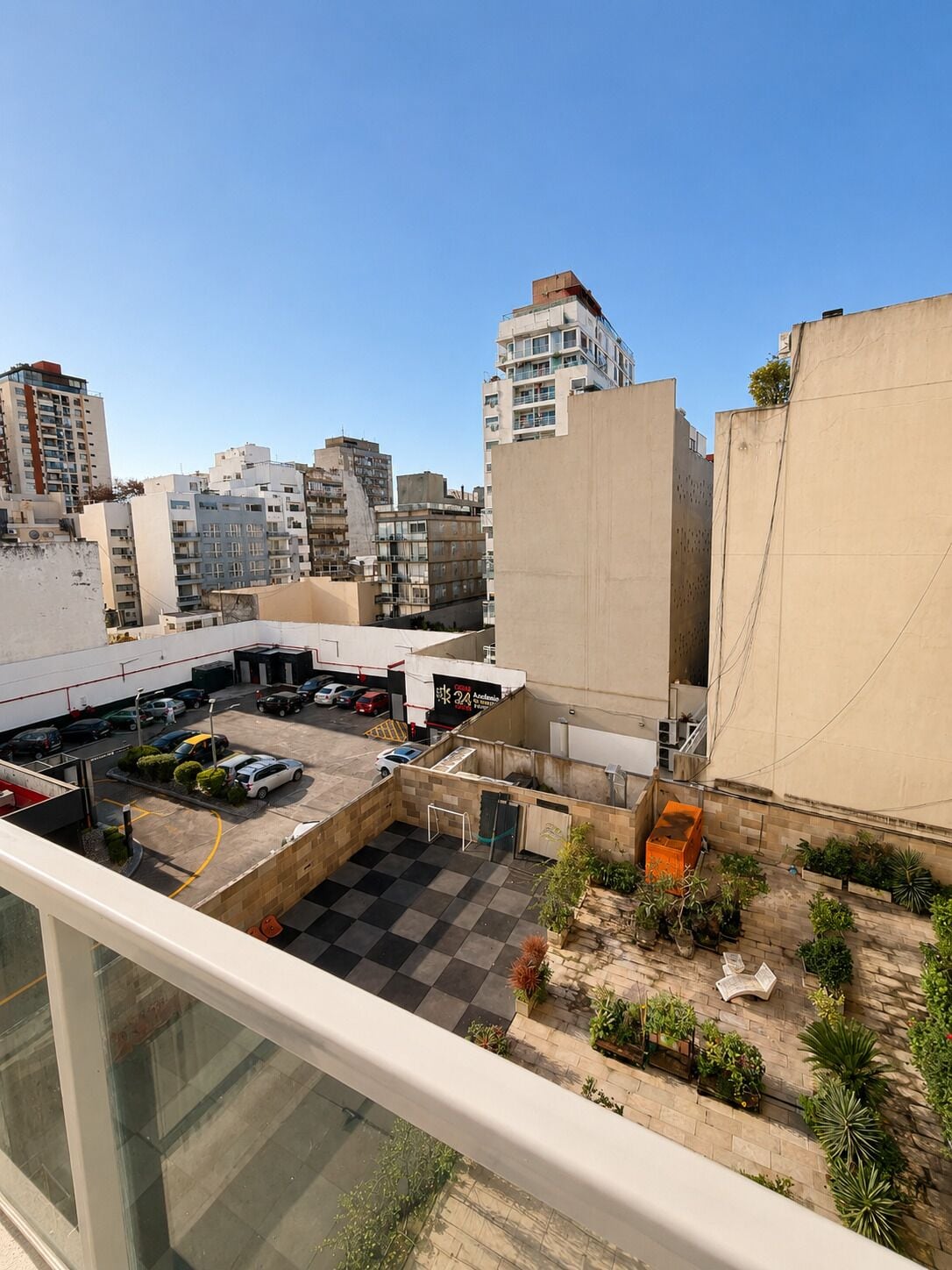 Terraço com área de estacionamento, um pequeno jardim e vista para edifícios ao redor.