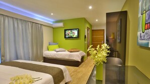 Quarto de hotel com duas camas, televisão, escrivaninha e uma parede verde de destaque.