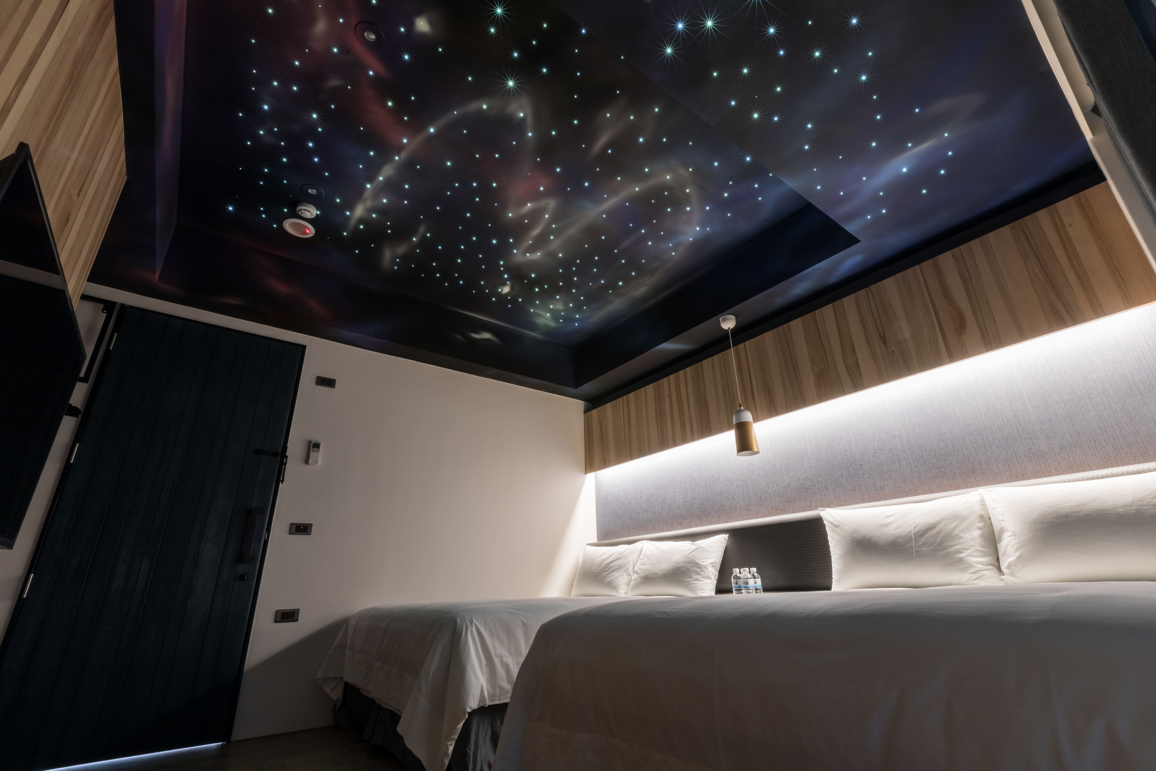 Quarto com cama, mesa de cabeceira e teto com design de céu estrelado.