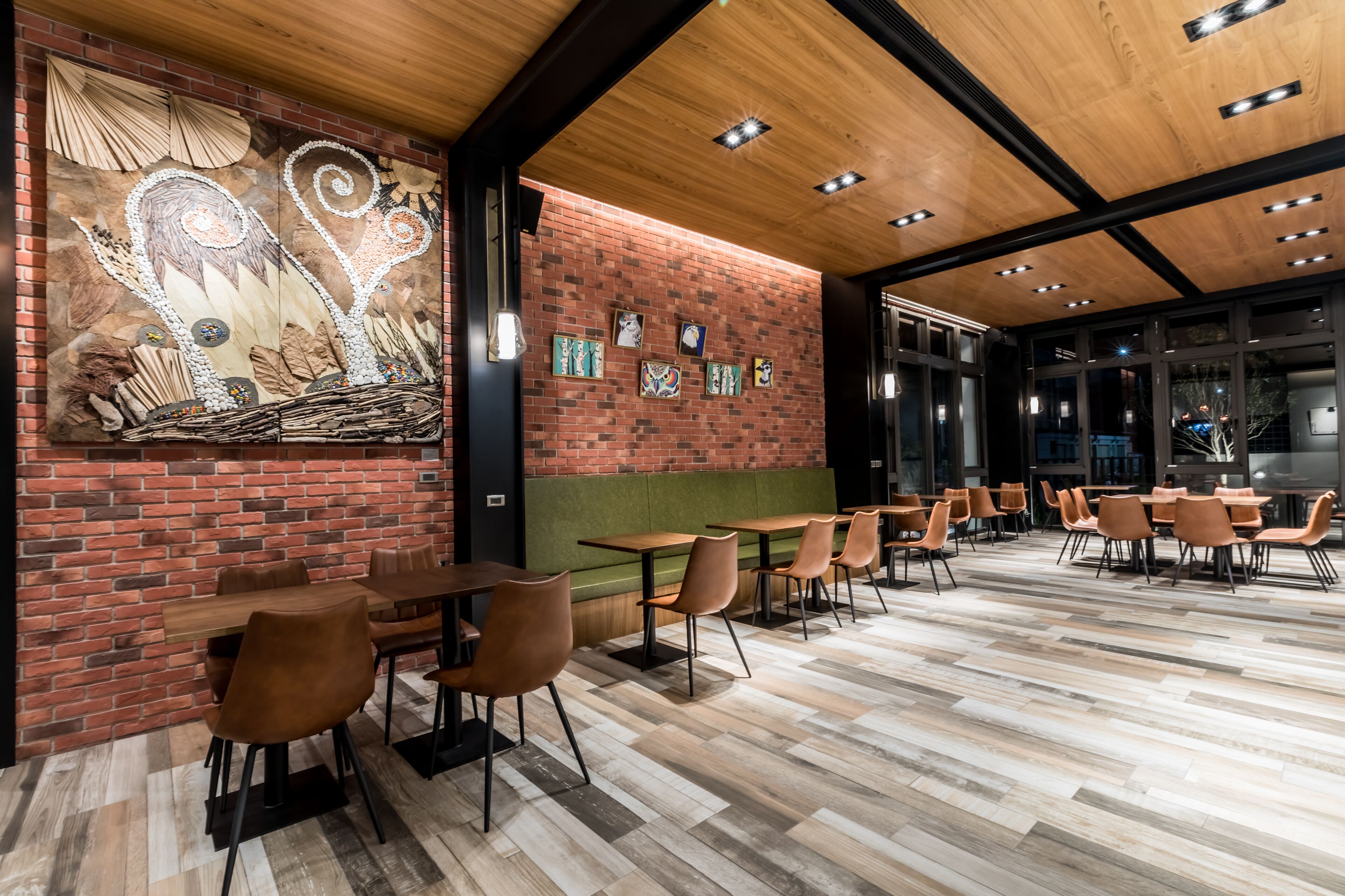Restaurante moderno com paredes de tijolo, piso de madeira e área de assentos em cabines verdes.