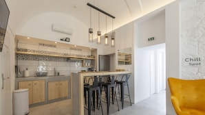 Uma cozinha moderna com uma ilha central, banquetas e uma cadeira amarela.