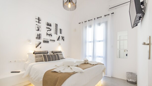 Um quarto moderno com uma cama grande, obras de arte na parede, uma televisão e uma janela com cortinas.