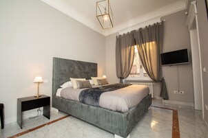 Um quarto moderno com uma cama grande, uma mesa de cabeceira, um abajur, uma TV na parede e uma janela com cortinas.