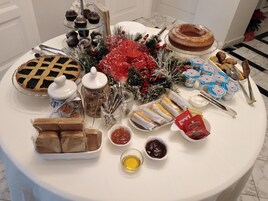 Uma mesa com diversos alimentos, incluindo tortas, doces e acompanhamentos, dispostos sobre uma toalha de mesa branca.