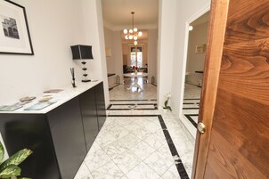 Um corredor com piso de mármore, porta de madeira e um balcão de recepção com abajur preto e quadro emoldurado.