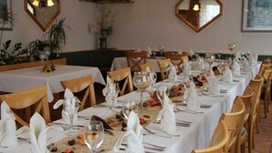 Uma longa mesa de jantar posta com toalhas brancas, cadeiras e arranjos organizados, incluindo copos de vinho, pratos e talheres.