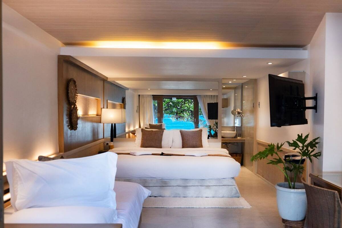 Quarto de hotel moderno com uma cama grande, área de estar, banheiro e vista para uma piscina.
