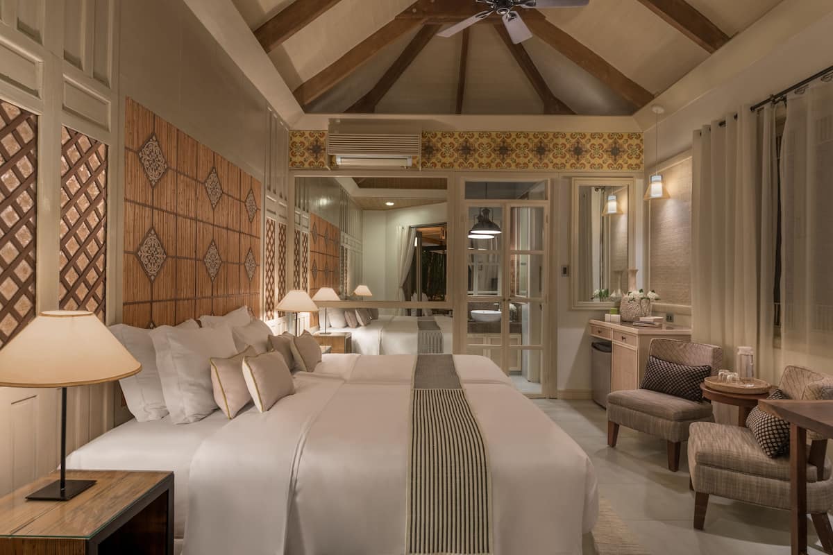 Um quarto espaçoso com uma cama grande, mesas de cabeceira e um espaço de estar com cadeiras.