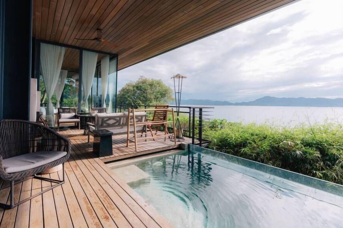 Piscina infinita com espreguiçadeiras de madeira e vista para um lago.