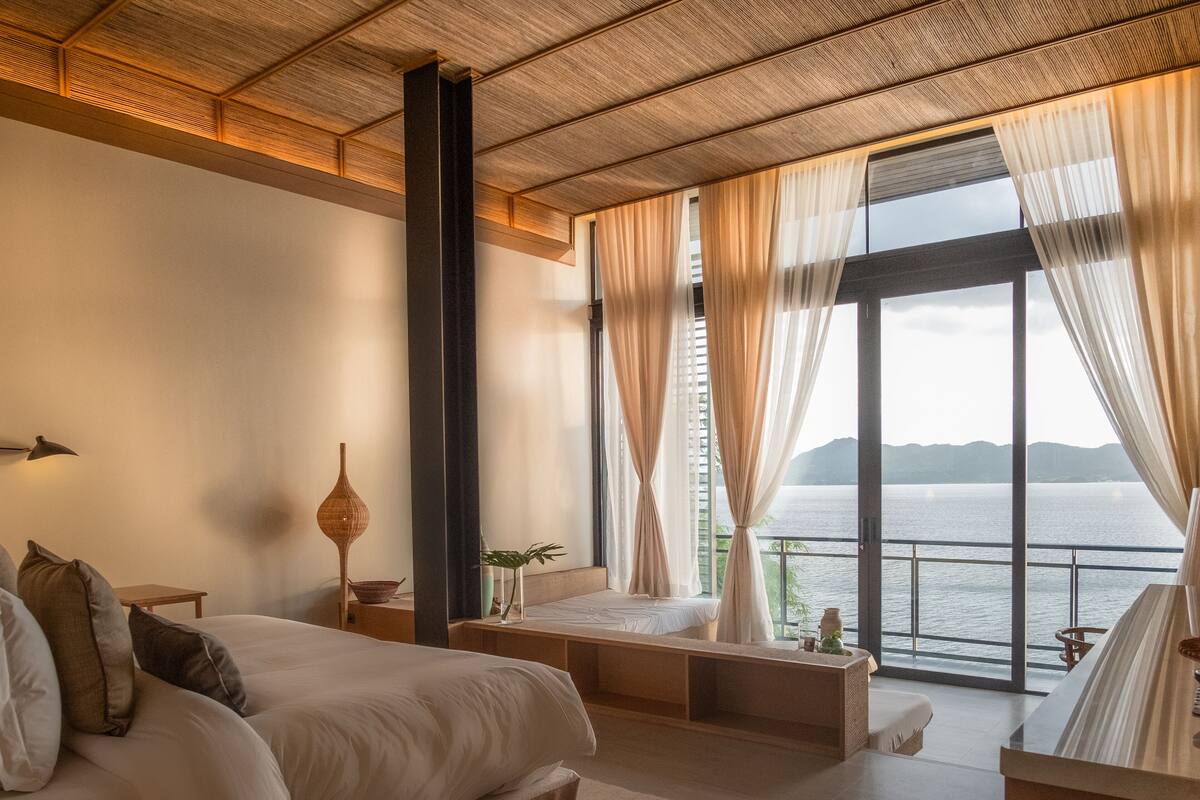Quarto com uma janela grande, uma cama, uma mesa de cabeceira e um criado-mudo.