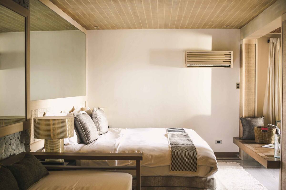 Quarto moderno com cama, mesa de cabeceira, abajur e um espelho grande.