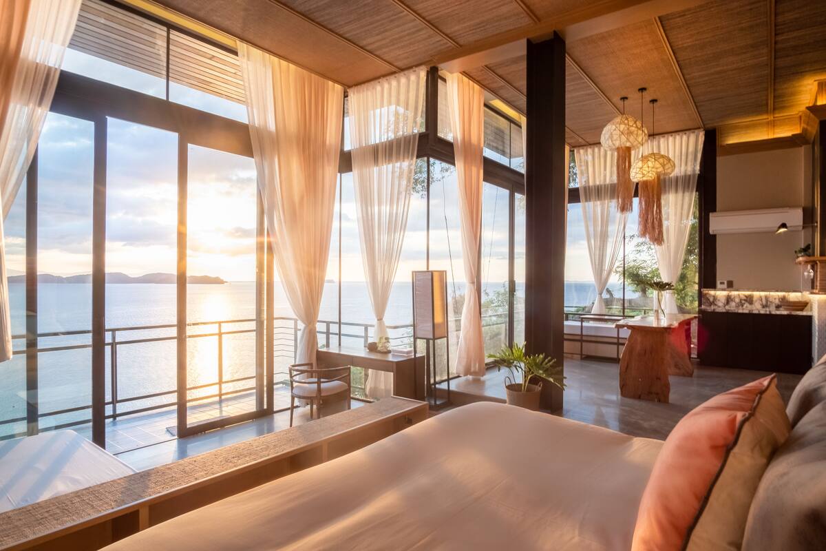 Um quarto espaçoso com uma cama grande, uma escrivaninha e vista para o mar.