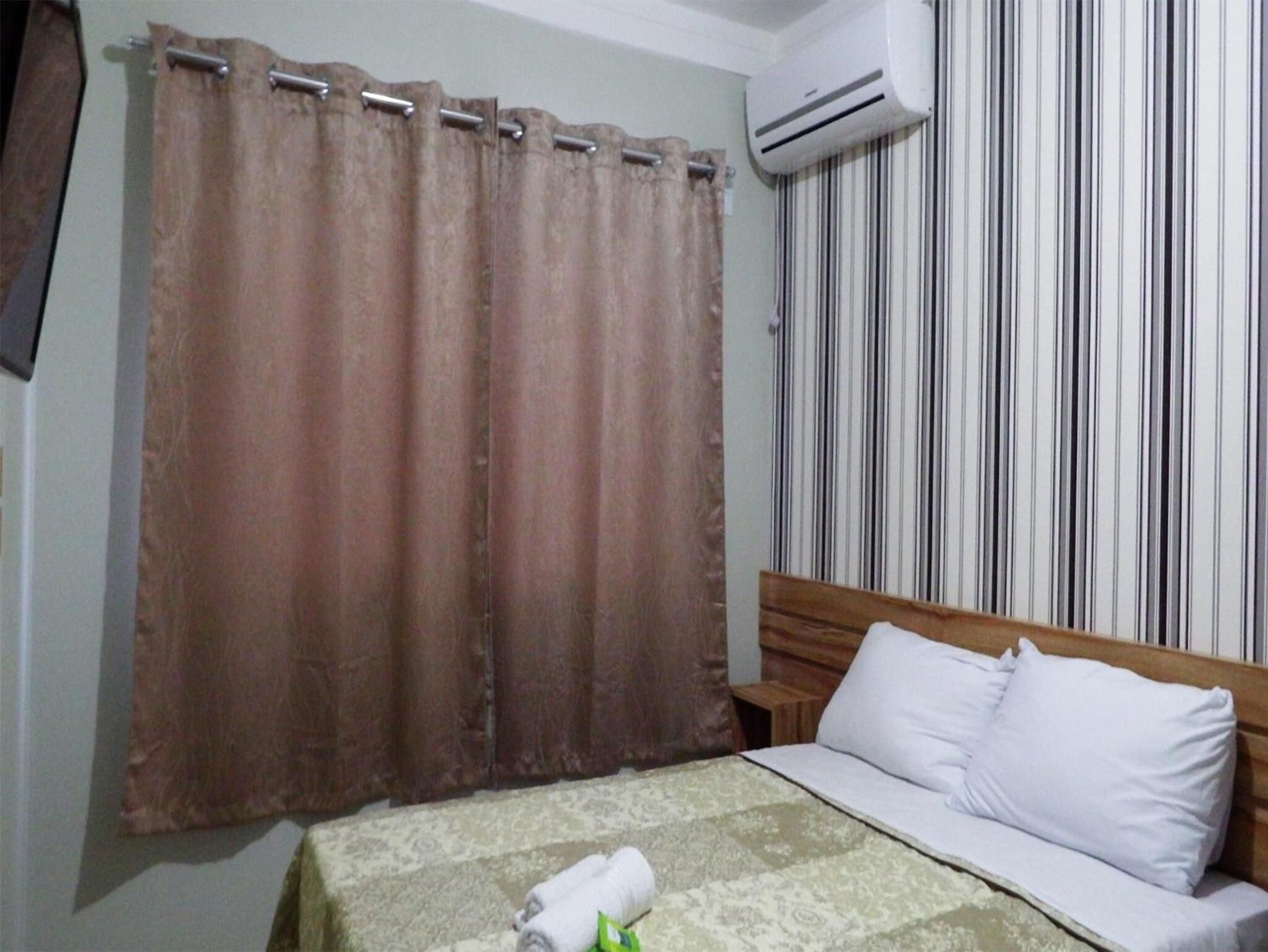 Quarto com uma cama, cabeceira de madeira, parede listrada e aparelho de ar condicionado.