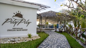 Placa indicando 'Pity Pity Restaurant and Andilana Beach Resort', com um caminho que leva a uma área coberta com cadeiras e mesas.