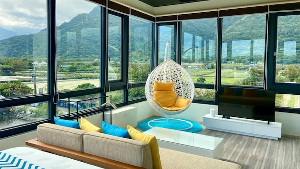 Quarto moderno com grandes janelas, uma cadeira suspensa, um sofá e uma TV.