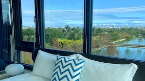 Quarto com uma grande janela, um sofá branco e vista para um lago e paisagem urbana.