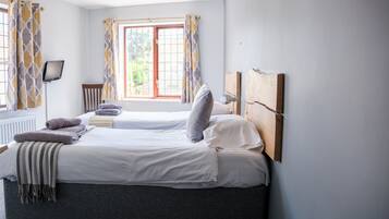 Quarto com duas camas, televisão e janela com cortinas.