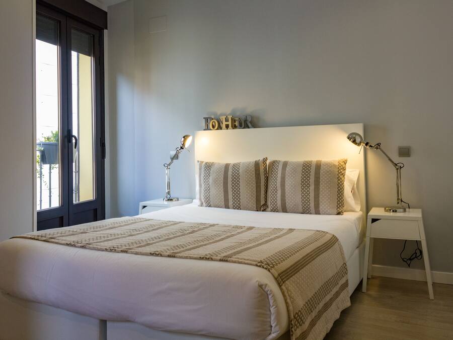 Quarto com cama, mesas de cabeceira, luminárias e uma janela.