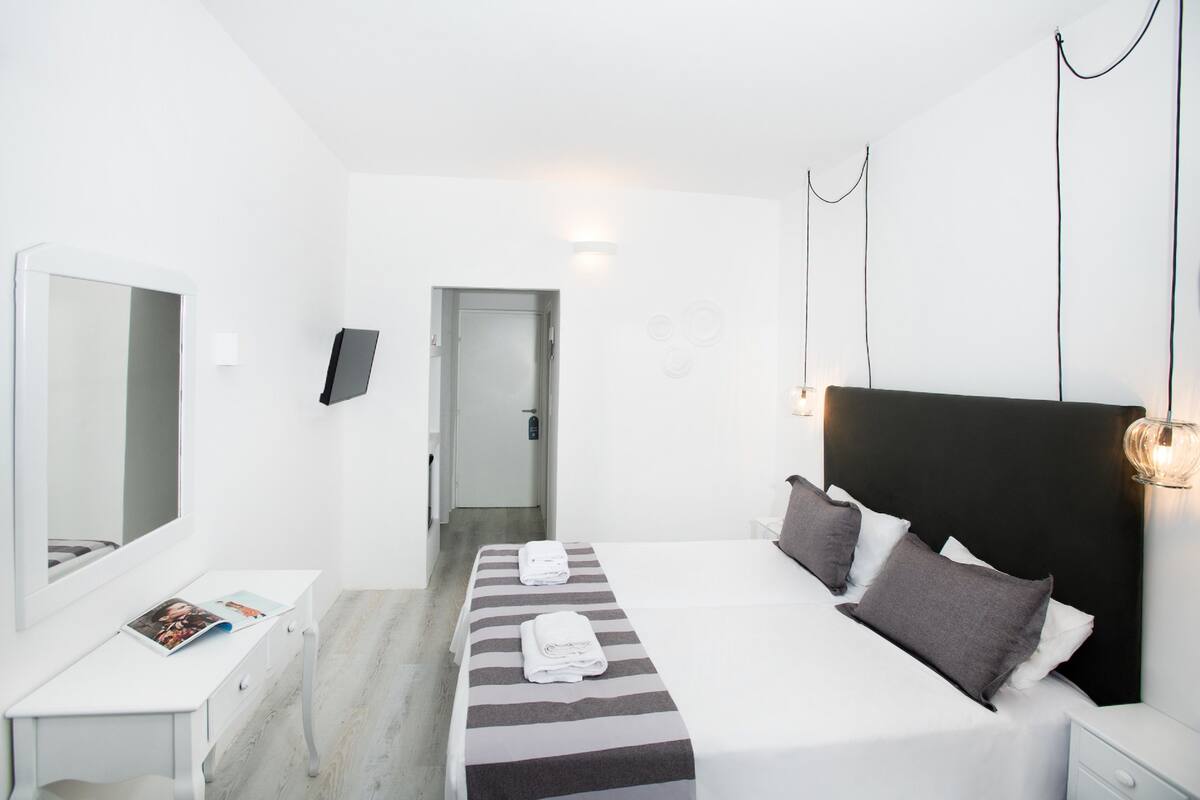 Quarto de hotel moderno com uma cama grande, mesa de cabeceira, espelho e televisão.