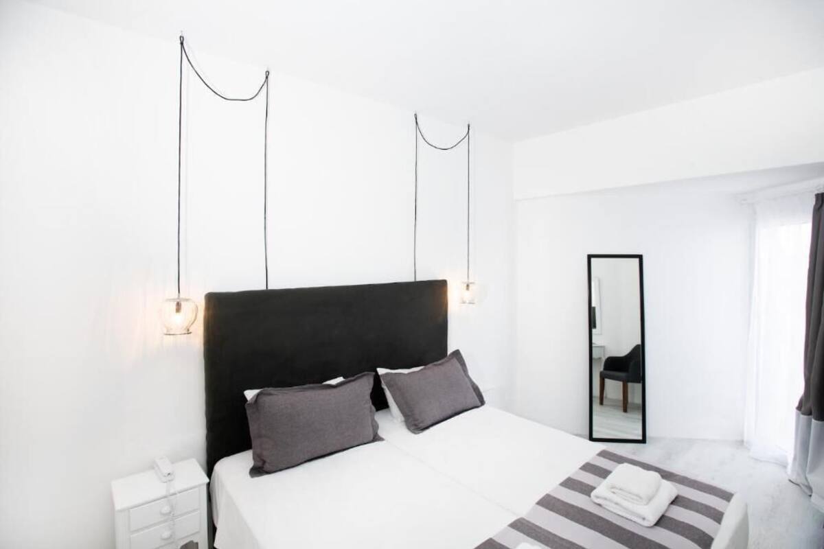 Quarto de hotel moderno com uma cama grande, mesas de cabeceira, um espelho e vista para o banheiro.