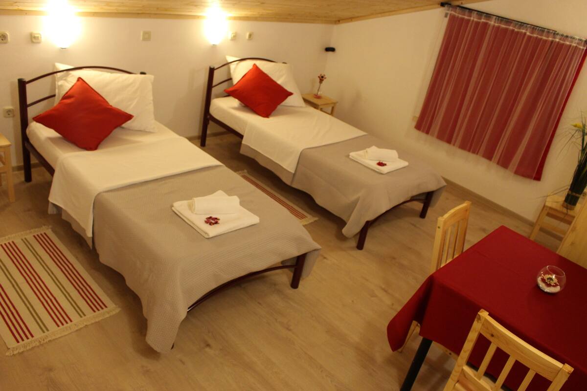 Quarto com duas camas de solteiro, uma mesa de madeira com toalha vermelha e uma cadeira.