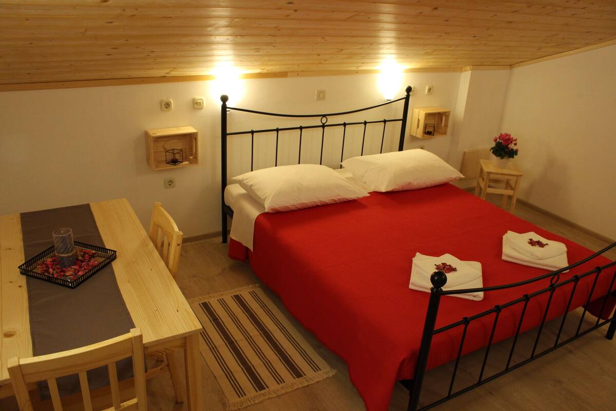 Quarto com cama, mesa de madeira e cadeira. Possui duas mesas de cabeceira com abajures.