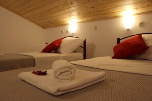 Quarto de hotel com duas camas, cada uma com almofada vermelha e roupa de cama branca. Há uma toalha enrolada na cama em primeiro plano.